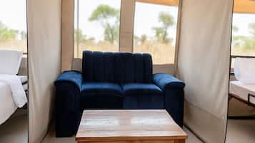 Um espaço de estar acolhedor com um sofá azul escuro e uma mesa de madeira, rodeado por cortinas bege e vista para o exterior.