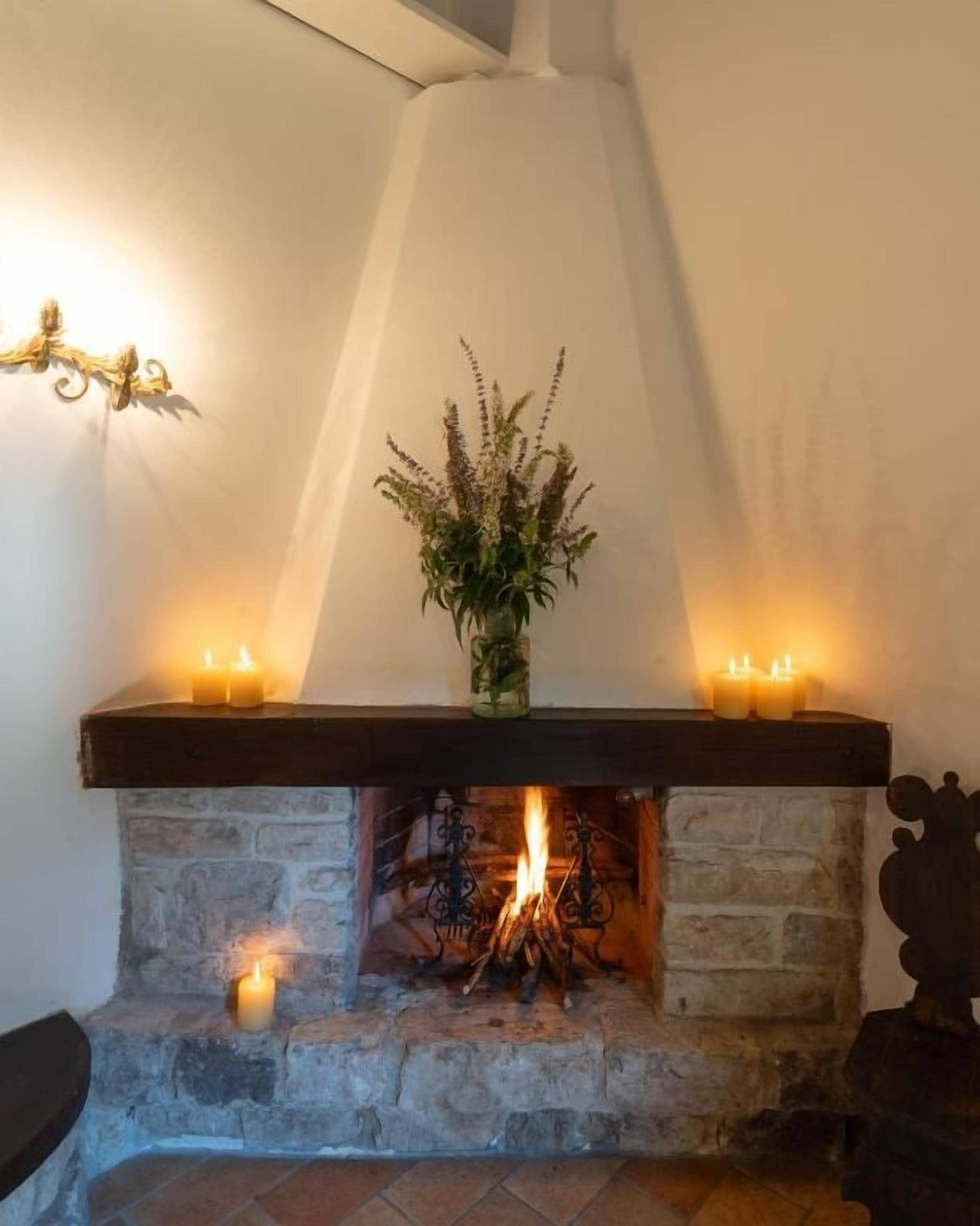 Lareira com revestimento de pedra, vaso com plantas e velas.