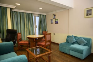 Uma sala de estar com mesa de centro de madeira, duas poltronas, um sofá e uma mesa de jantar com cadeiras.