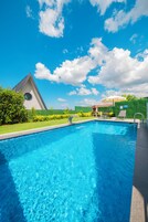 Piscina com água azul cristalina, rodeada por um jardim bem cuidado e um edifício com um telhado triangular característico.