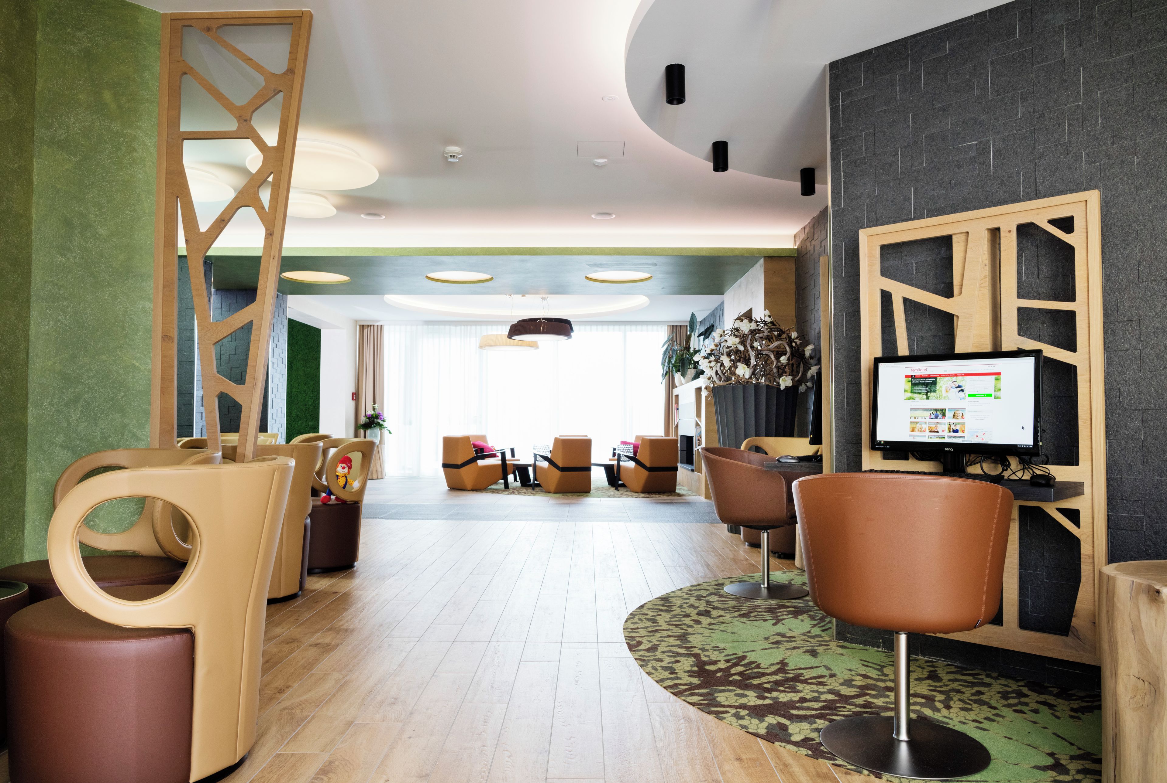 Um lobby de hotel moderno com balcão de recepção, área de estar e uma tela grande exibindo conteúdo.