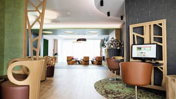 Um lobby de hotel moderno com balcão de recepção, área de estar e uma tela grande exibindo conteúdo.