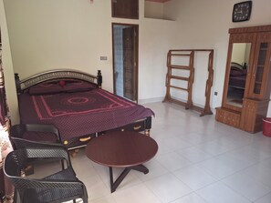 Quarto com cama, guarda-roupa de madeira, mesa redonda, duas cadeiras e espelho.