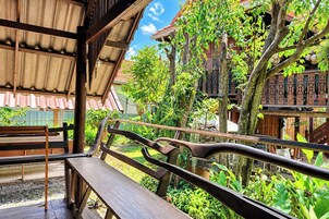 Um banco de madeira sob uma cobertura, com vista para um jardim e edifícios tradicionais.