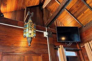 Teto de madeira com um candeeiro pendurado e uma televisão fixada na parede.