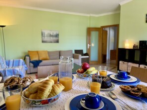 Mesa posta para dois com croissants, doces, frutas e bebidas para o café da manhã.