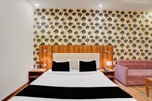 Quarto de hotel com cama, cabeceira de madeira, sofá rosa e papel de parede floral.