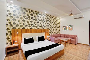 Quarto de hotel com cama grande, sofá rosa, mesinha e parede com papel de parede floral.