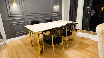 Uma sala de jantar com mesa e cadeiras de madeira, parede cinza com lambris e duas luminárias fixadas na parede.