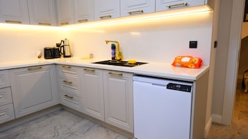 Cozinha moderna com armários brancos, máquina de lavar louça embutida e bancada com diversos eletrodomésticos.