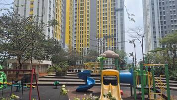 Um parquinho com diversos equipamentos de recreação, cercado por árvores e edifícios ao fundo.