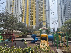 Um parquinho com diversos equipamentos de recreação, cercado por árvores e edifícios ao fundo.
