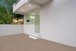 Design arquitetônico moderno com entrada por porta de vidro e um conjunto de degraus brancos que levam a uma área coberta.