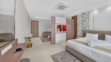 Quarto de hotel moderno com cama, escrivaninha, sofá e televisão.