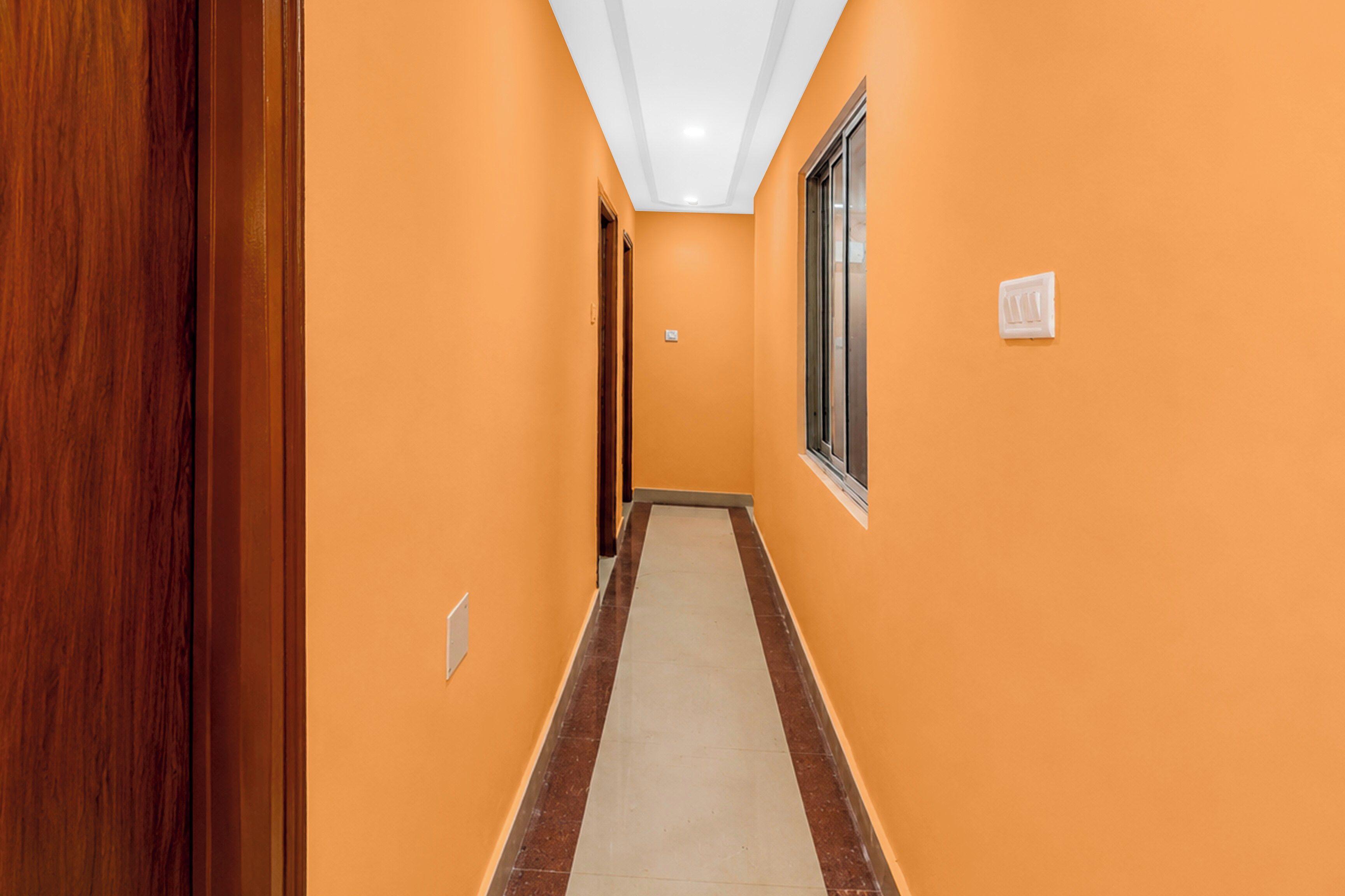 Um corredor com paredes laranja, uma porta de madeira à esquerda e uma janela à direita.