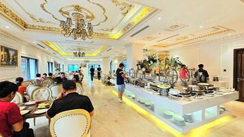Espaço de refeições de hotel com decoração de teto elaborada, balcão de buffet e hóspedes a jantar.