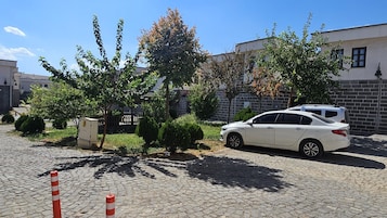 Um carro branco estacionado numa rua de calçada, com árvores e um edifício ao fundo.