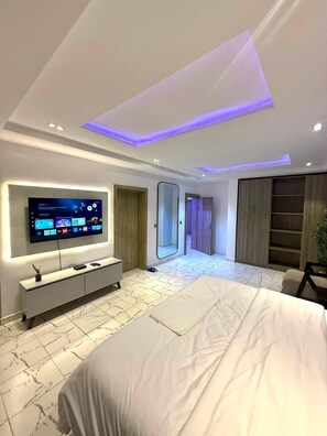 Quarto moderno com cama grande, televisão montada na parede e closet espaçoso.