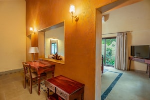 Quarto de hotel com escrivaninha de madeira, espelho, televisão e vista para área verde.