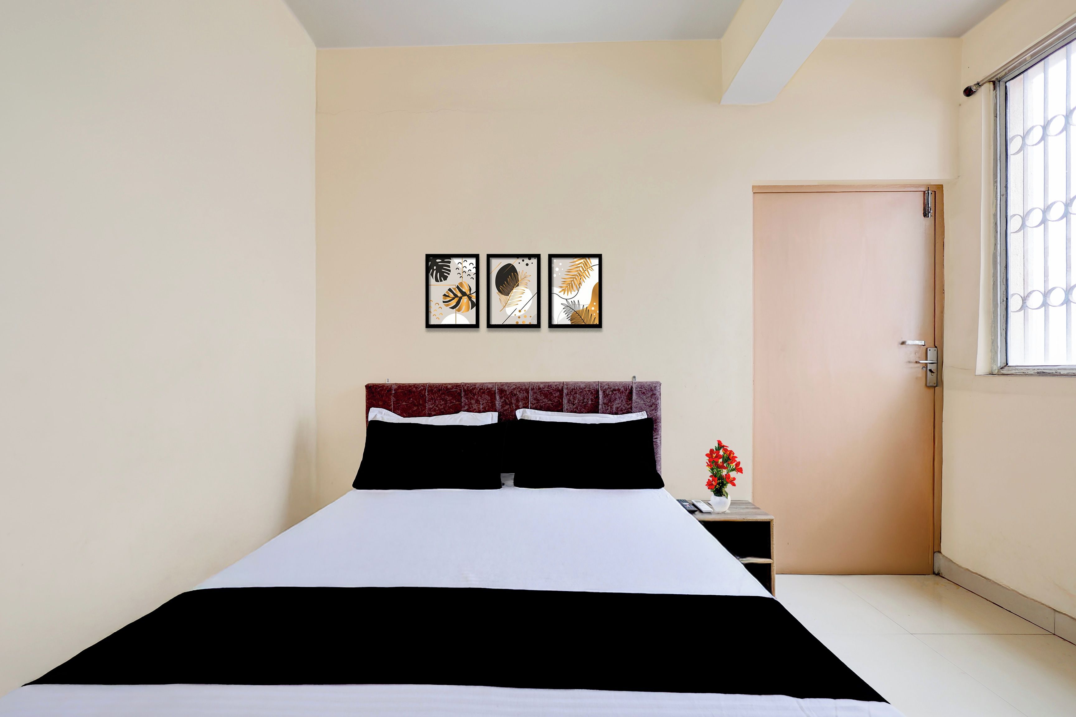 Quarto de hotel com cama, mesa de cabeceira, porta e três quadros pendurados na parede.