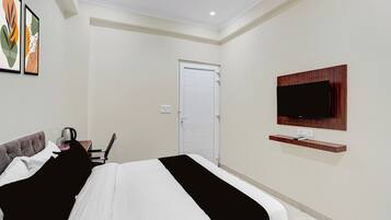 Quarto de hotel com uma cama, televisão presa na parede, uma porta e uma pequena prateleira com controle remoto.