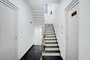 Um corredor estreito com paredes brancas, escadaria de mármore e portas de ambos os lados.