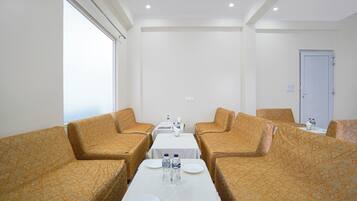 Quarto de hotel com uma mesa comprida, dois sofás, uma porta e uma janela.