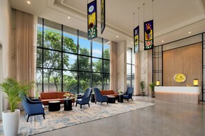 Um hall espaçoso com balcão de recepção, área de estar e amplas janelas com vista para o verde.