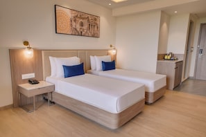 Quarto de hotel com duas camas, uma mesa de cabeceira, escrivaninha e um quadro na parede.