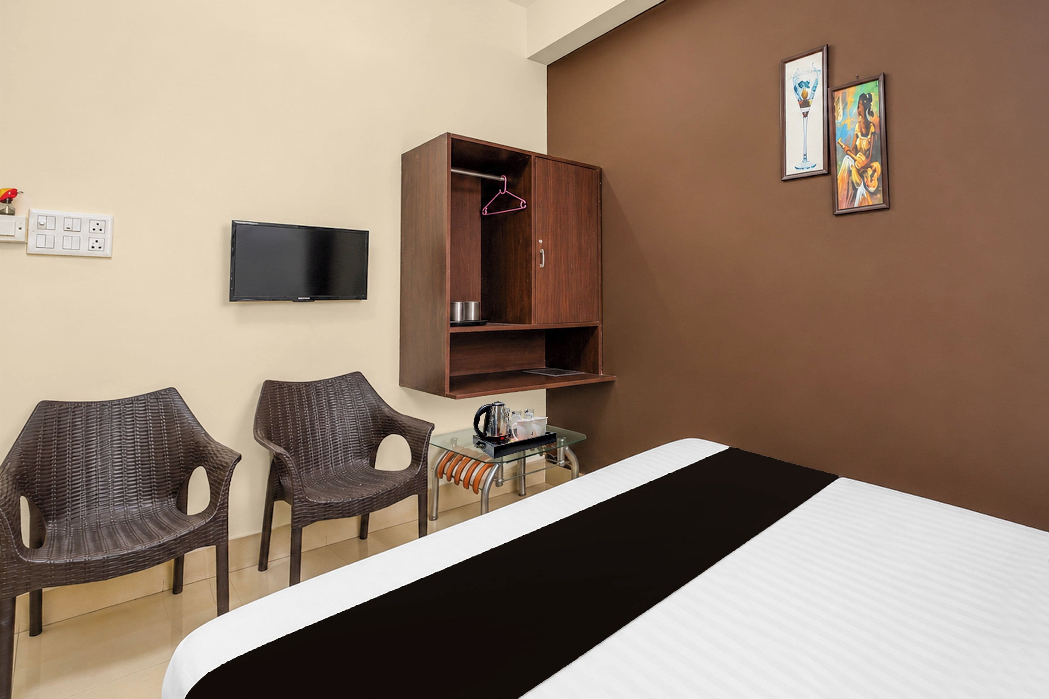 Quarto de hotel com uma cama, duas cadeiras, televisão, guarda-roupa e uma pequena mesa com chaleira.