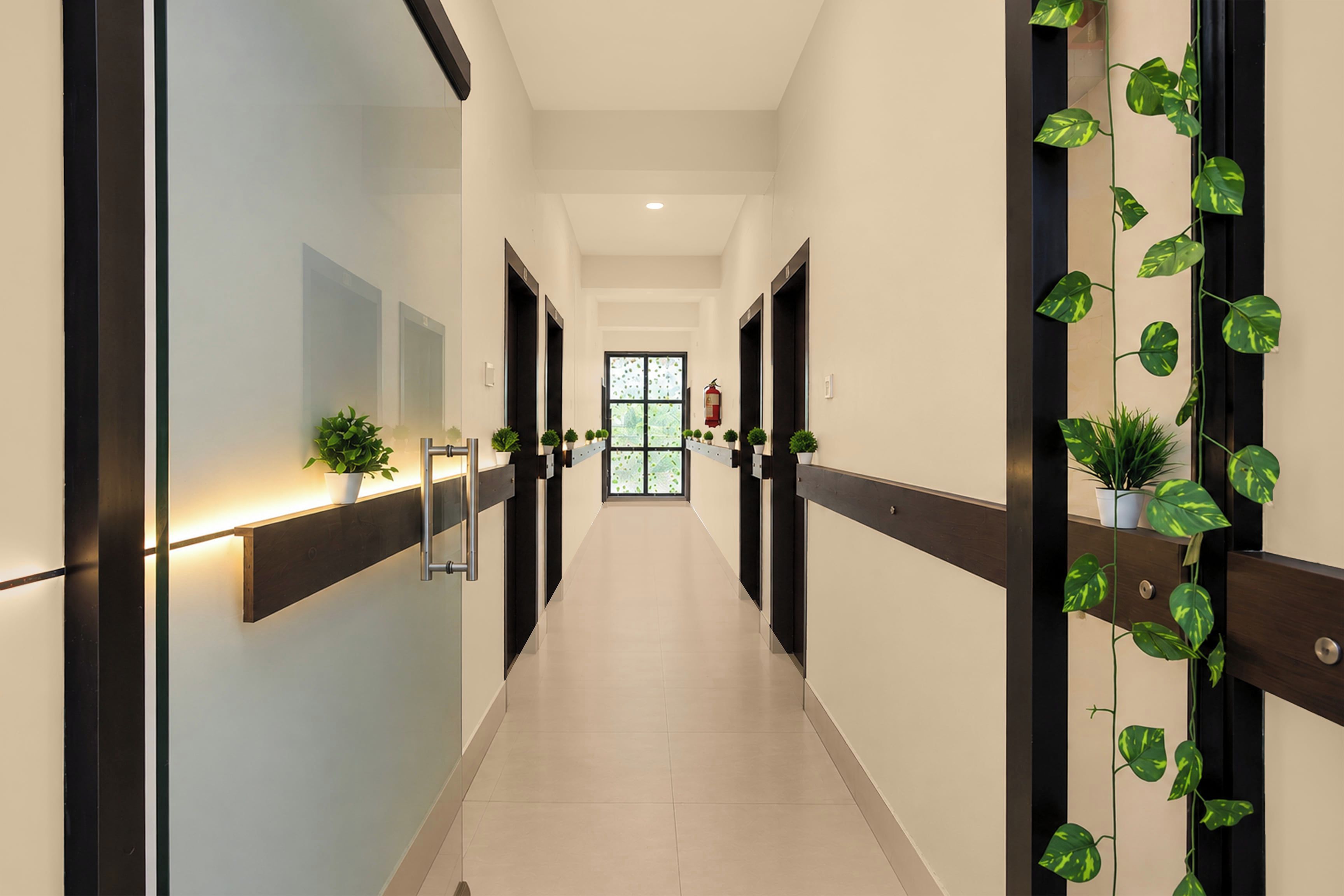 Um corredor moderno com piso claro, detalhes em madeira escura e plantas em vasos ao longo das paredes.