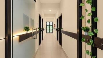Um corredor moderno com piso claro, detalhes em madeira escura e plantas em vasos ao longo das paredes.