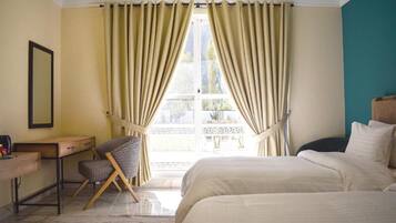 Quarto de hotel com cama, escrivaninha, cadeira e cortinas.