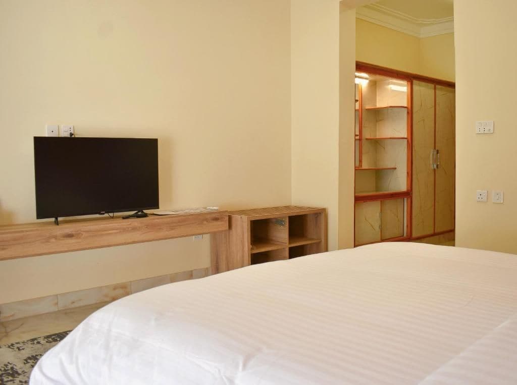 Quarto com cama, televisão sobre suporte de madeira e guarda-roupa com espelho.