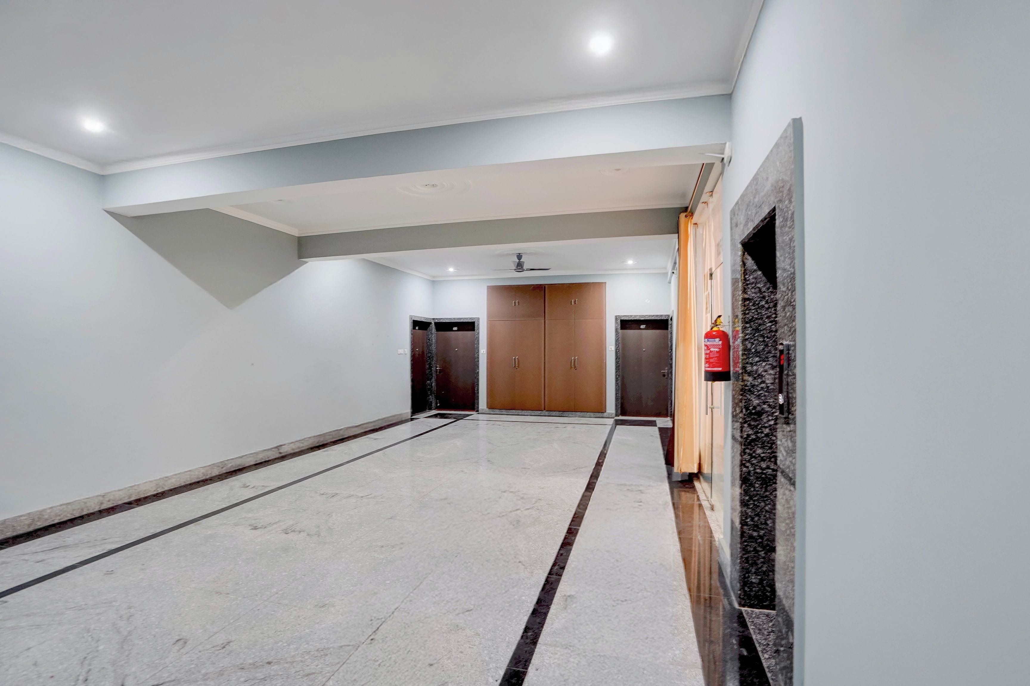 Um corredor amplo com piso de mármore, teto com iluminação embutida e um extintor de incêndio fixado na parede.