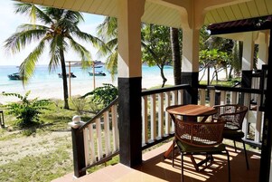 Varanda com vista para a praia e oceano, com uma mesa e cadeiras.