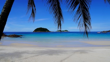 Uma praia com águas azul-claras, areal arenoso e palmeiras.