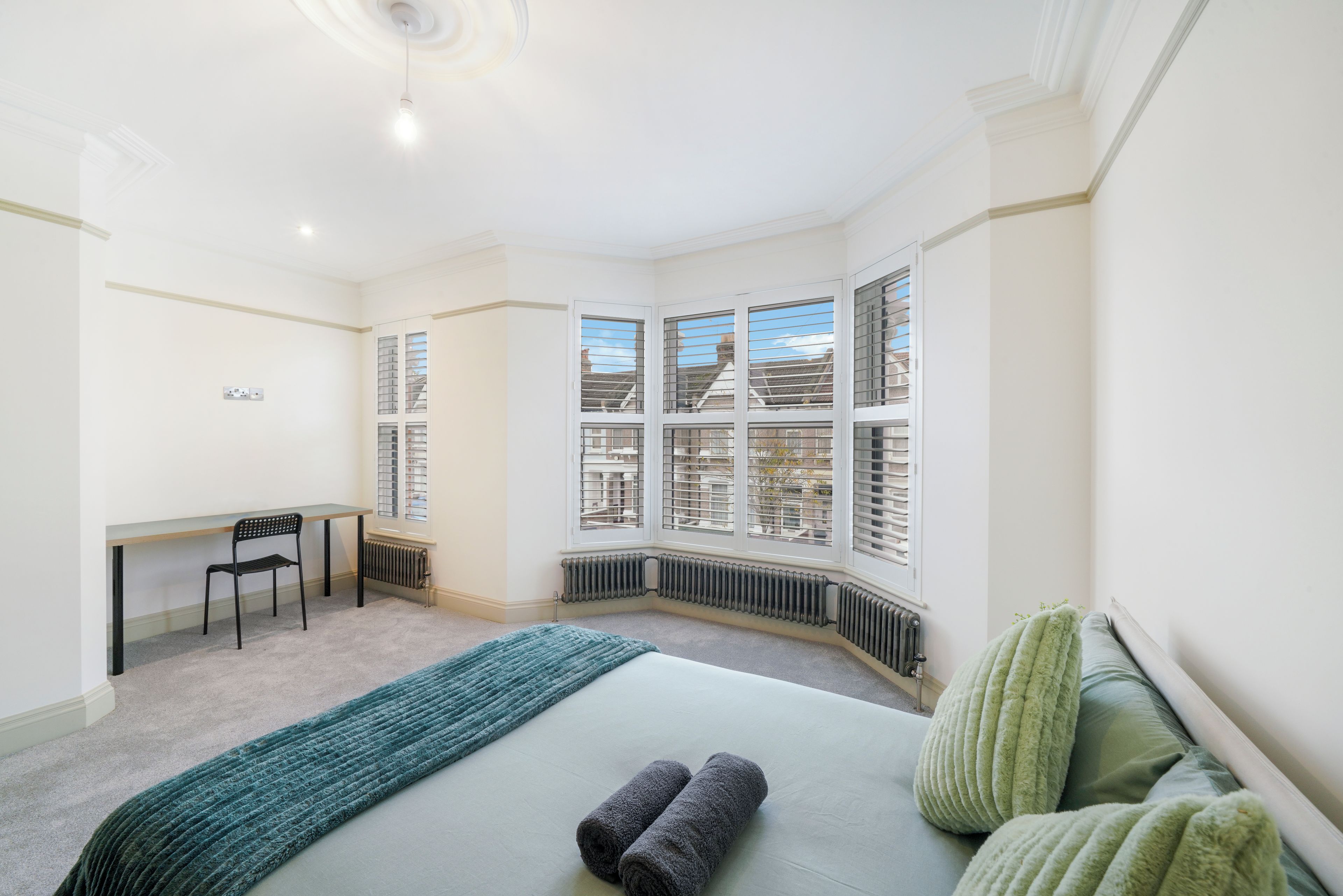 Quarto com cama, escrivaninha e vista exterior por um janela em arco.