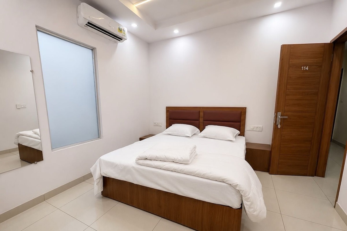 Quarto de hotel com uma cama, porta de madeira e janela.