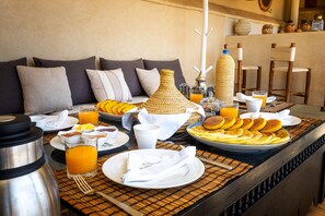 Buffet de café da manhã com diversos pratos, uma cafeteira e uma garrafa de suco de laranja sobre uma mesa.