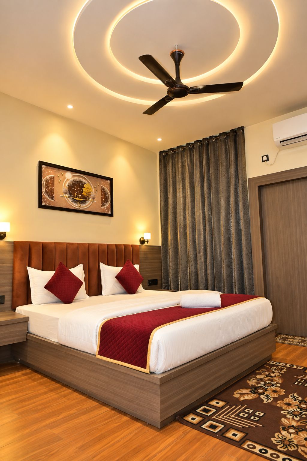 Quarto de hotel com cama, ventilador de teto, ar condicionado fixado na parede e um objeto decorativo na parede.