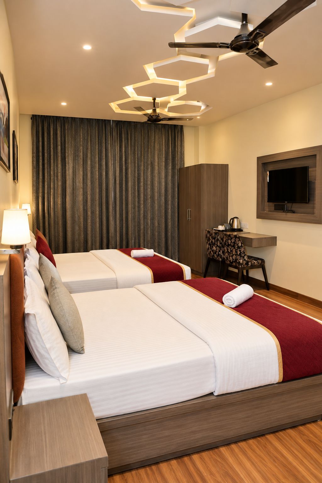 Quarto de hotel com duas camas, uma escrivaninha, televisão e luminária no teto.