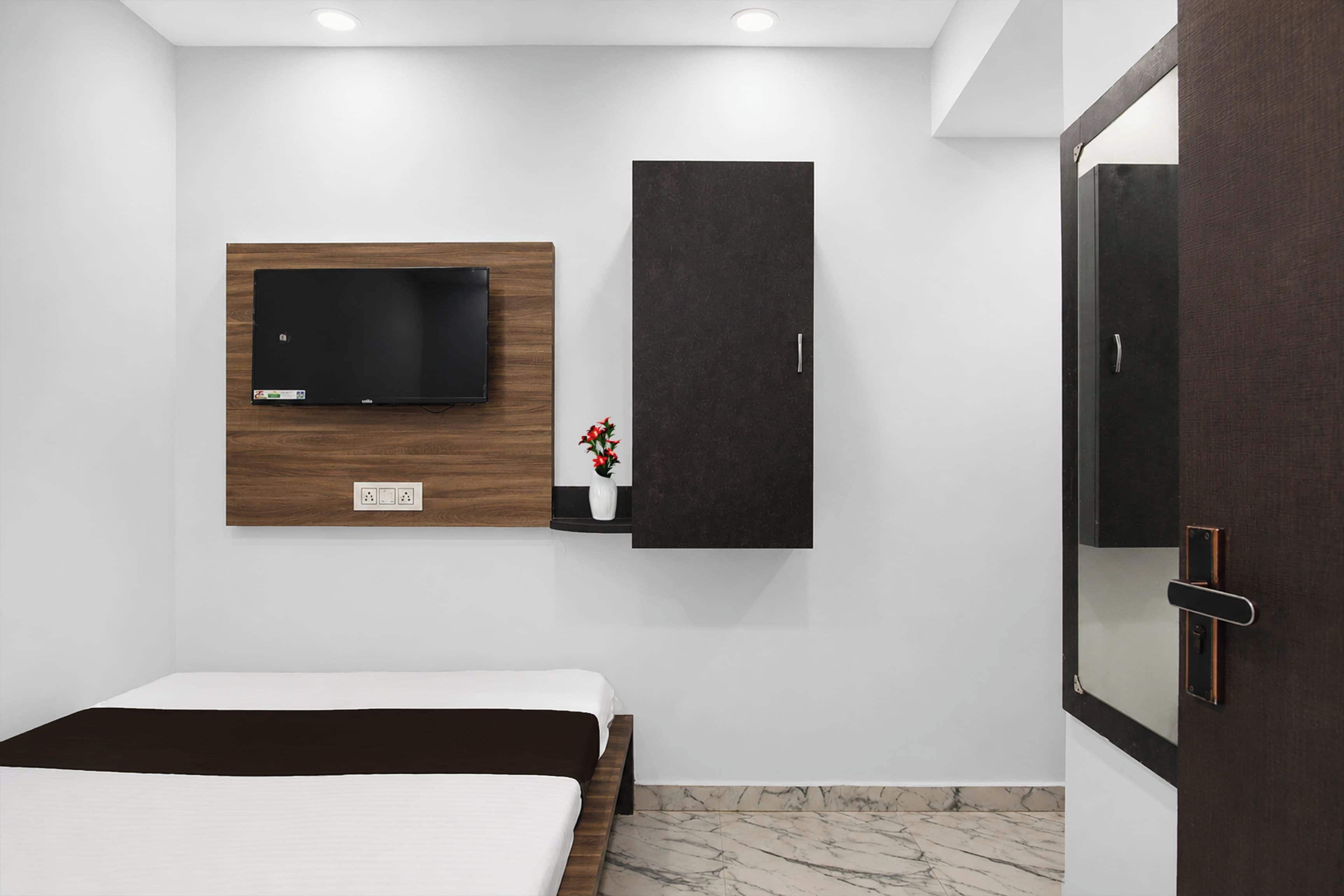 Quarto com cama, televisão na parede, guarda-roupa e porta com espelho.