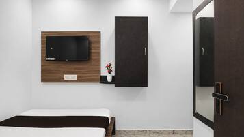 Quarto com cama, televisão na parede, guarda-roupa e porta com espelho.