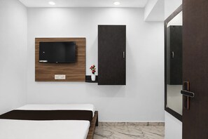 Quarto com cama, televisão na parede, guarda-roupa e porta com espelho.