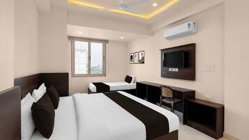 Quarto de hotel com cama, escrivaninha, cadeira, televisão e ar condicionado.