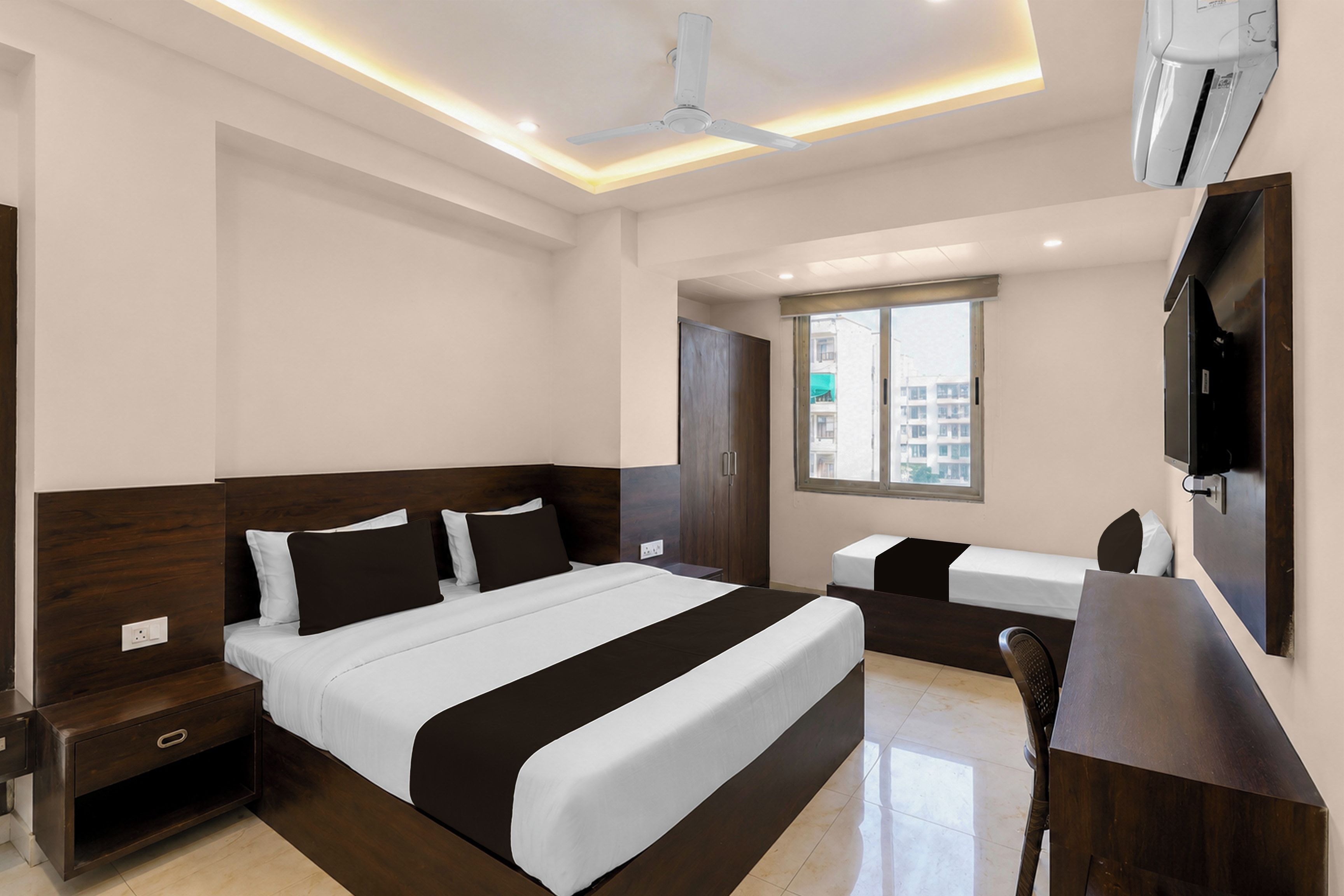 Quarto de hotel com uma cama grande, uma cama menor, uma escrivaninha e uma televisão.