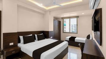 Quarto de hotel com uma cama grande, uma cama menor, uma escrivaninha e uma televisão.