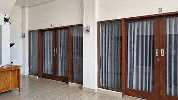 Quarto de hotel com piso de madeira, uma mesa de trabalho e duas grandes portas deslizantes com cortinas.