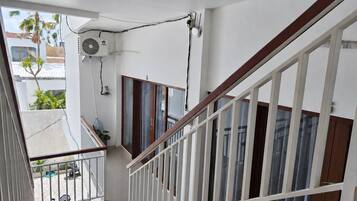 Varanda residencial com guarda-corpo de madeira, ventilador de teto e vista para um prédio vizinho.